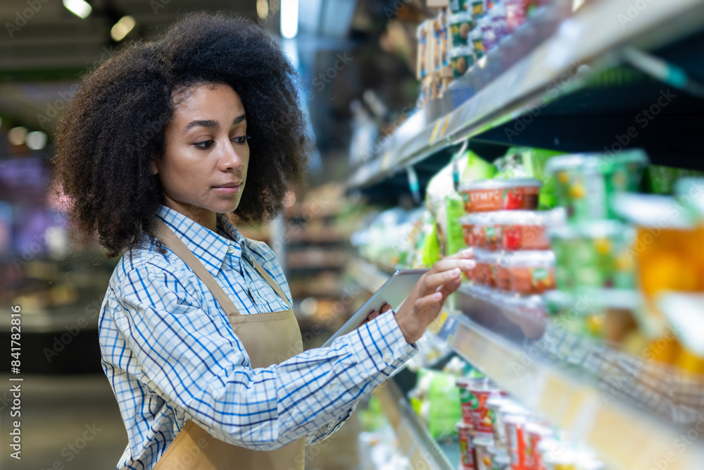 Young female grocery store worker using a tablet to manage inventory in ...