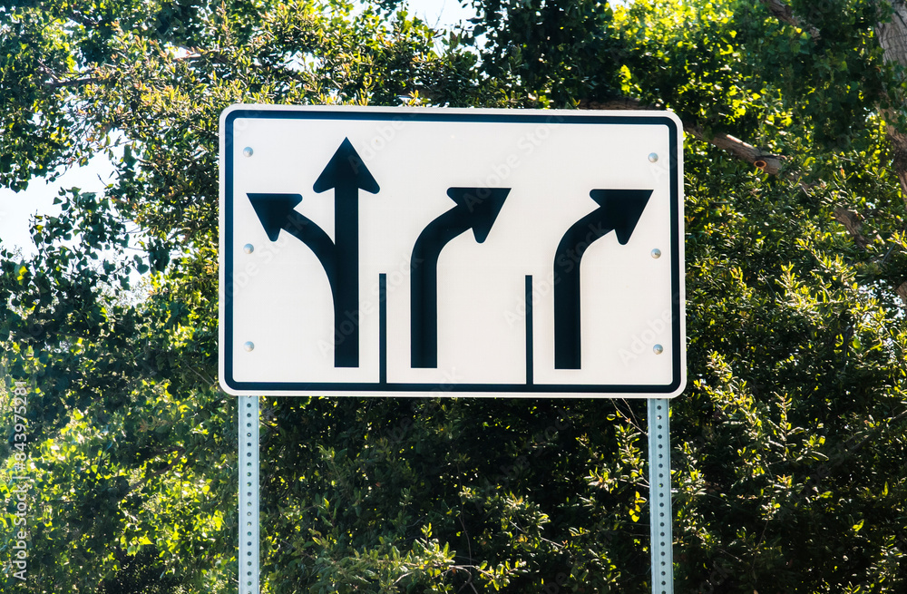 A white traffic sign with black arrows informing motorists of left turn ...