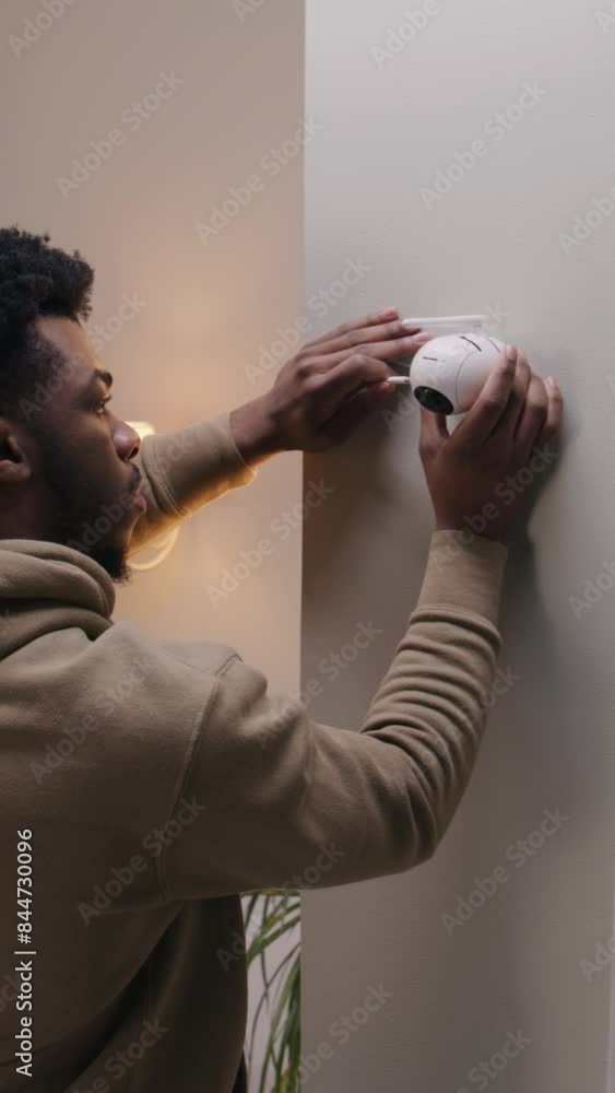 African American man puts security camera on wall fastening and ...