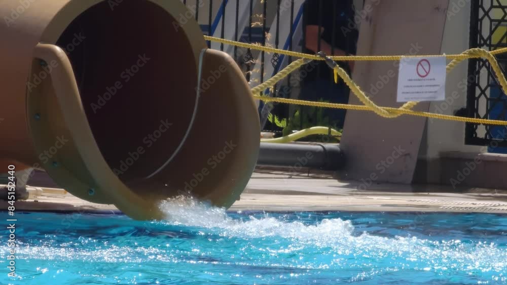 A close-up view of water slide as water pours from it into pool ...