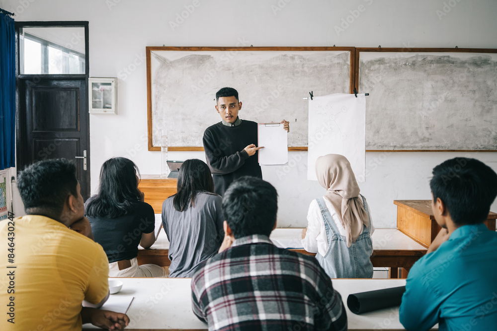 Teenager Students Listening To Young Male Teacher Explaining In Front ...