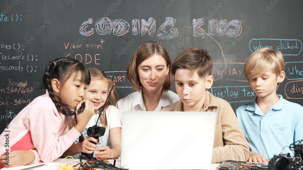 Diverse student writing engineering code while boy fixing mother board. Teacher giving advice ...