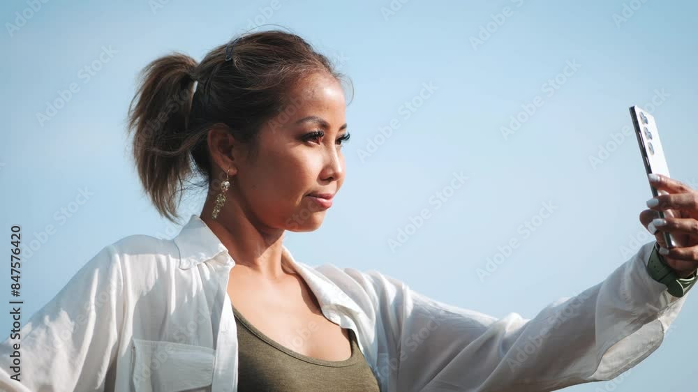 Young woman with tied-back hair takes selfie outdoors under a clear ...