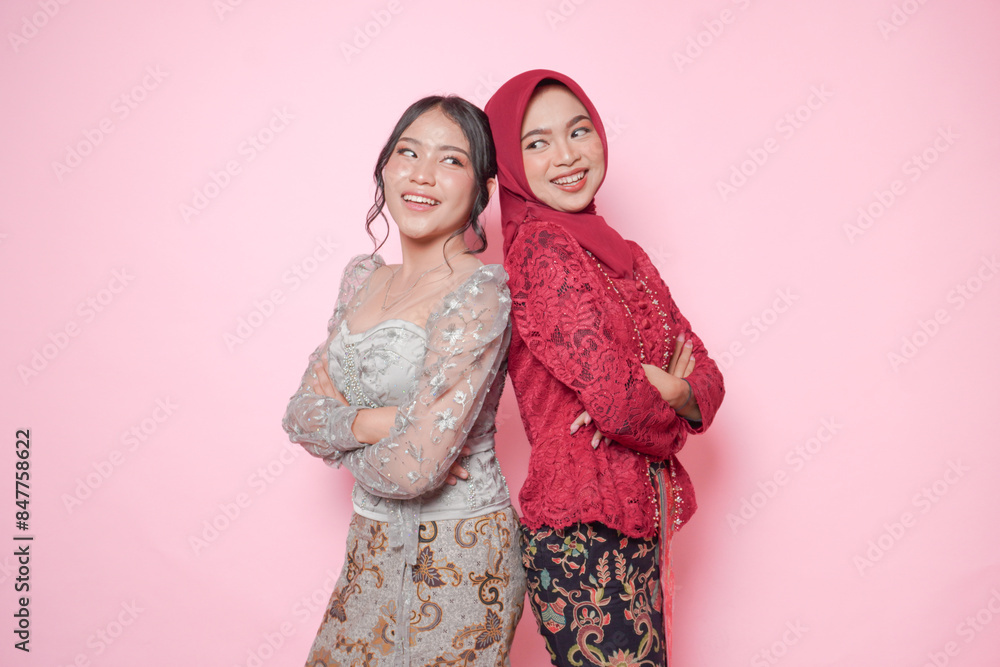 Two smiling Asian women wearing modern kebaya dress posing and leaning on each other back ...