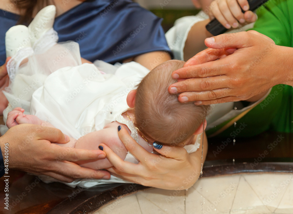Parents holding baby girl over baptismal font as priest performs water ...