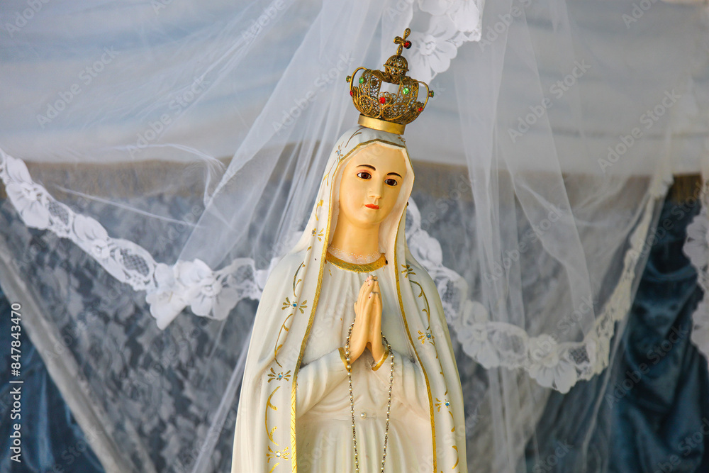 Statue of the virgin mary wearing a crown and praying under a white ...