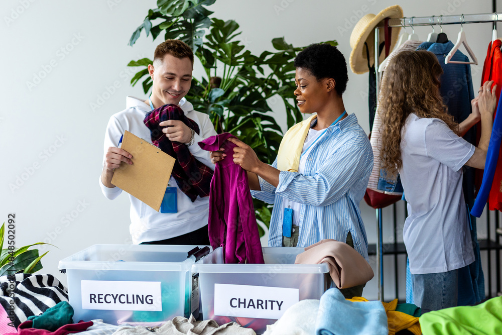 Group of volunteers, young women and man, sorting clothes in charitable ...