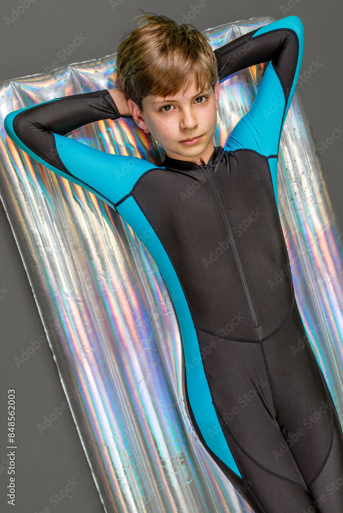 Boy in a rash guard wet suit floating on a colorful inflatable swimming ...