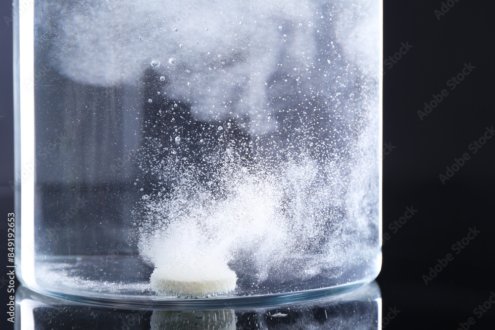Effervescent pill dissolving in glass of water on black background ...