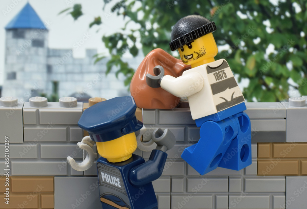 Lego minifigures of thief are climbing on brick wall and following ...