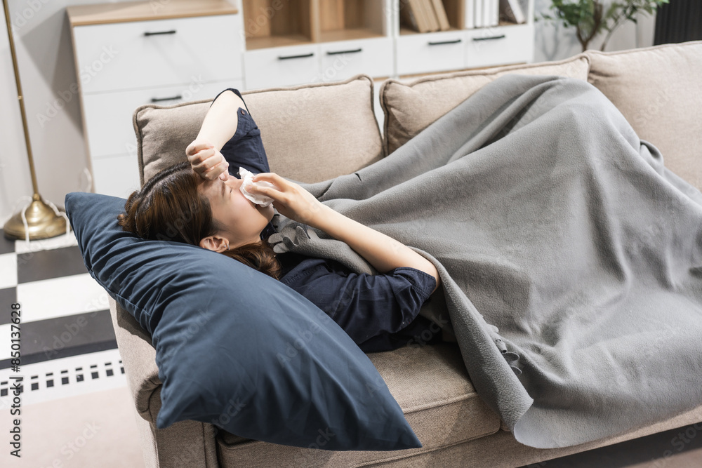 A young female Asian is resting on a sofa, suffering from the flu. She ...