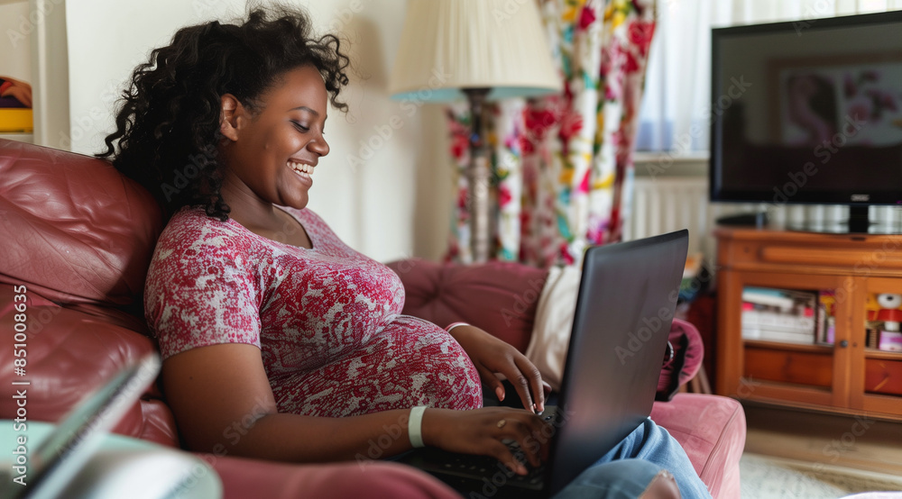 Happy pregnant black mom working remotely on laptop cradling baby bump ...