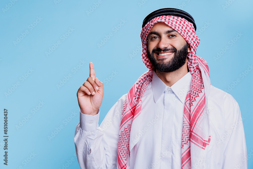 Smiling muslim man wearing arabic clothes pointing to upwards direction ...