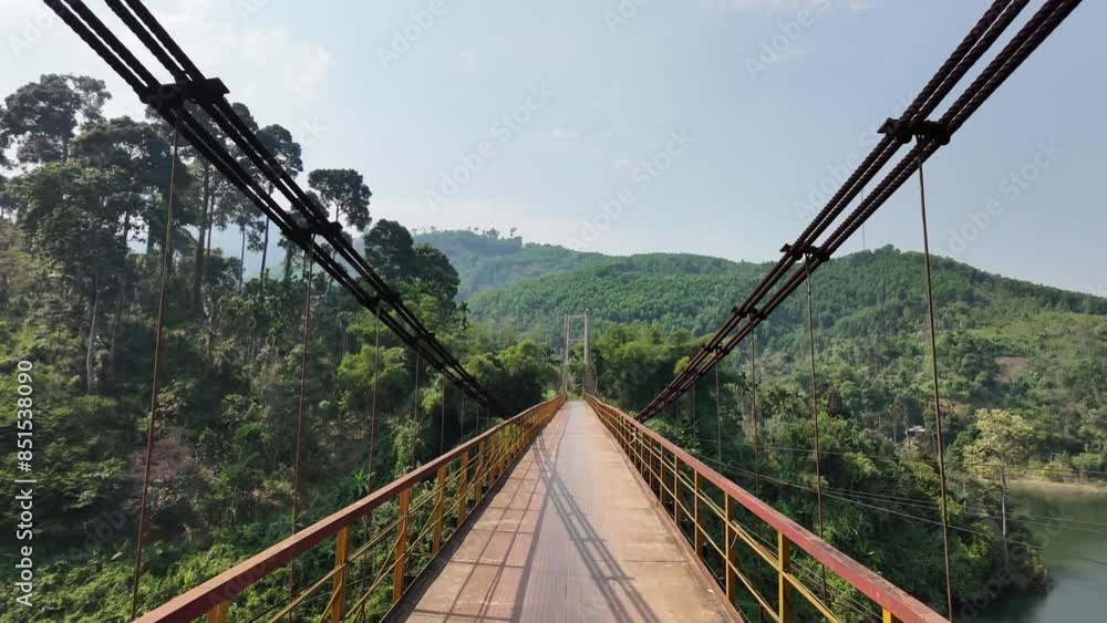 A suspension bridge stretches over lush green forests and hills during ...