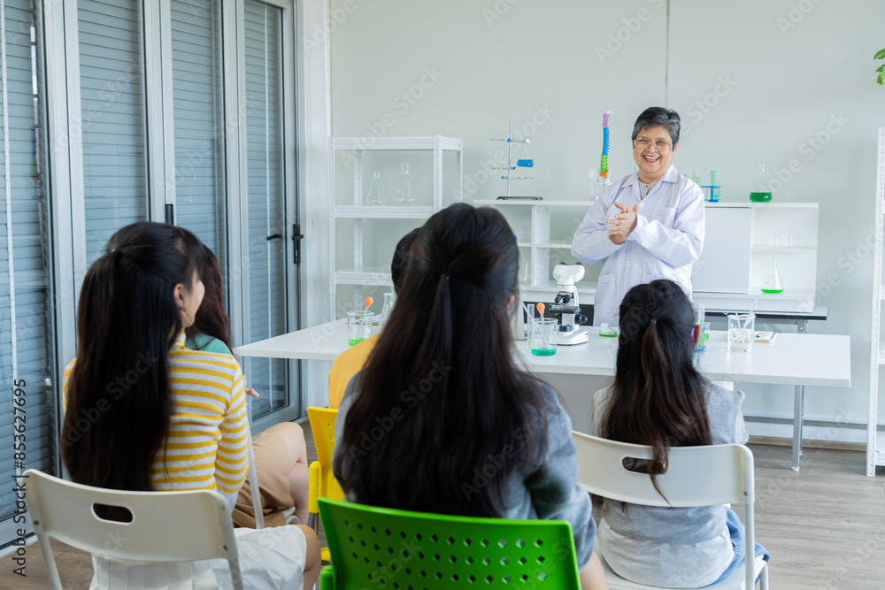 Senior teacher woman demonstrating microscope experiment to students in ...