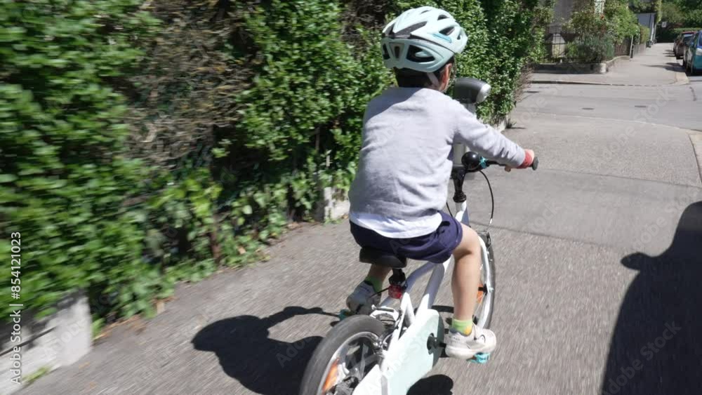 Back view of a child cycling along a sidewalk, showcasing the ...