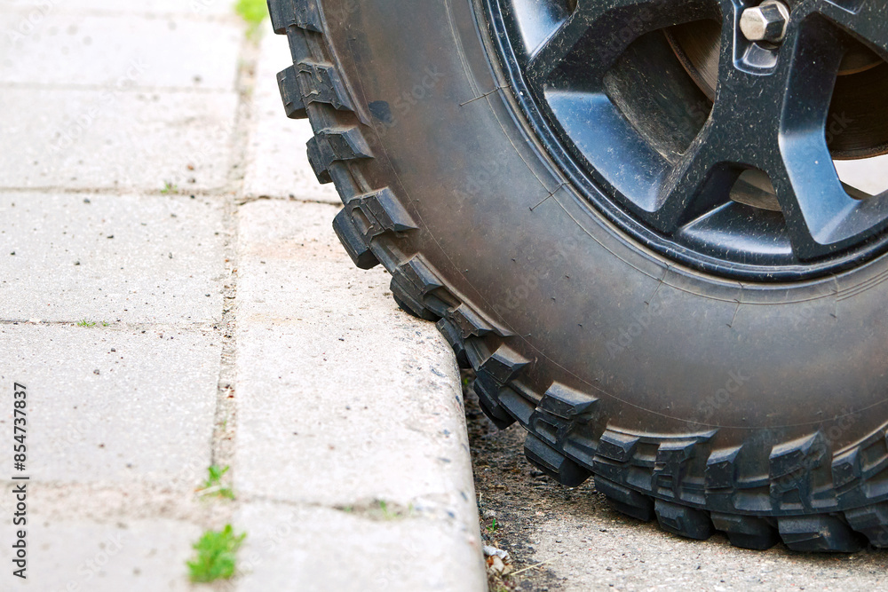 Extra large wheel tire next to the curb closeup. Extreme mud-terrain ...