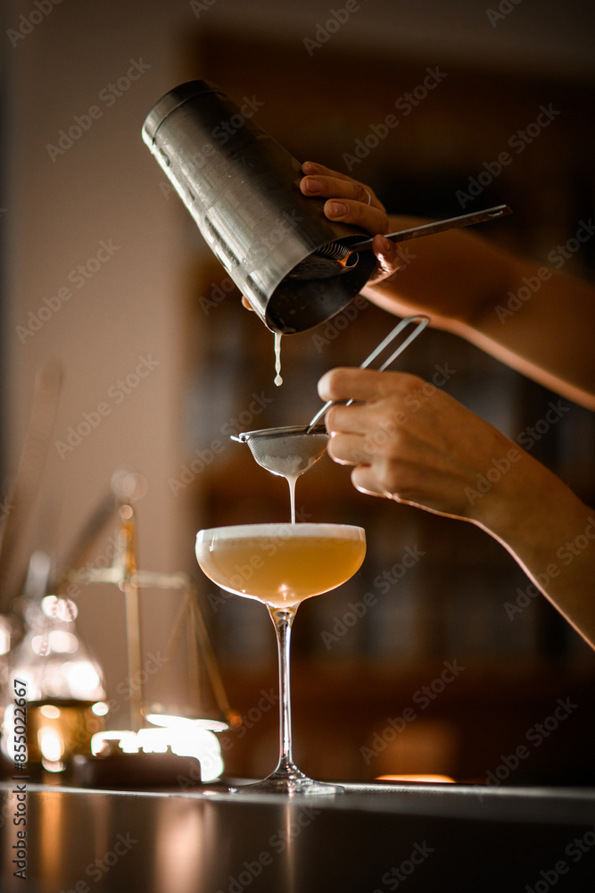 Female bartender finishes straining foamy champagne-colored cocktail ...
