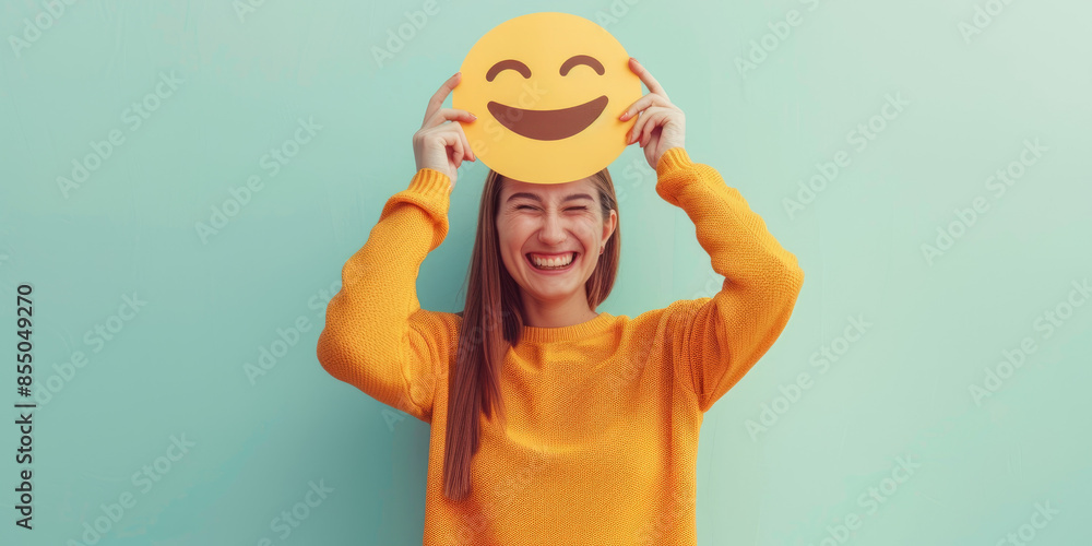 woman holding up an emoji face on pink background, smiley happy person ...