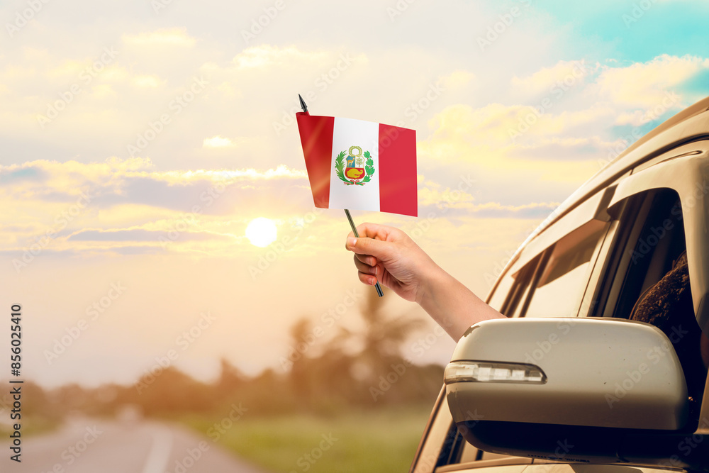 Waving the Peru flag against the sunrise or sunset from a car driving ...