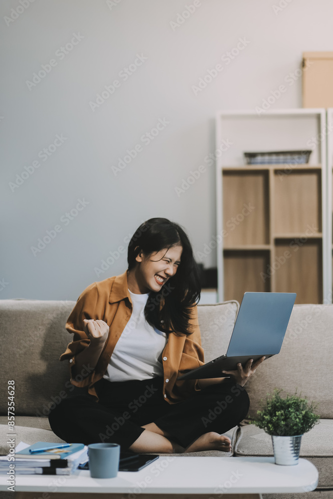 Emotional young asian woman in casual sitting on couch with laptop and ...