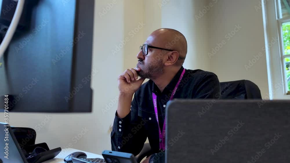 A man sits in front of a computer screen in an office setting, gazing ...