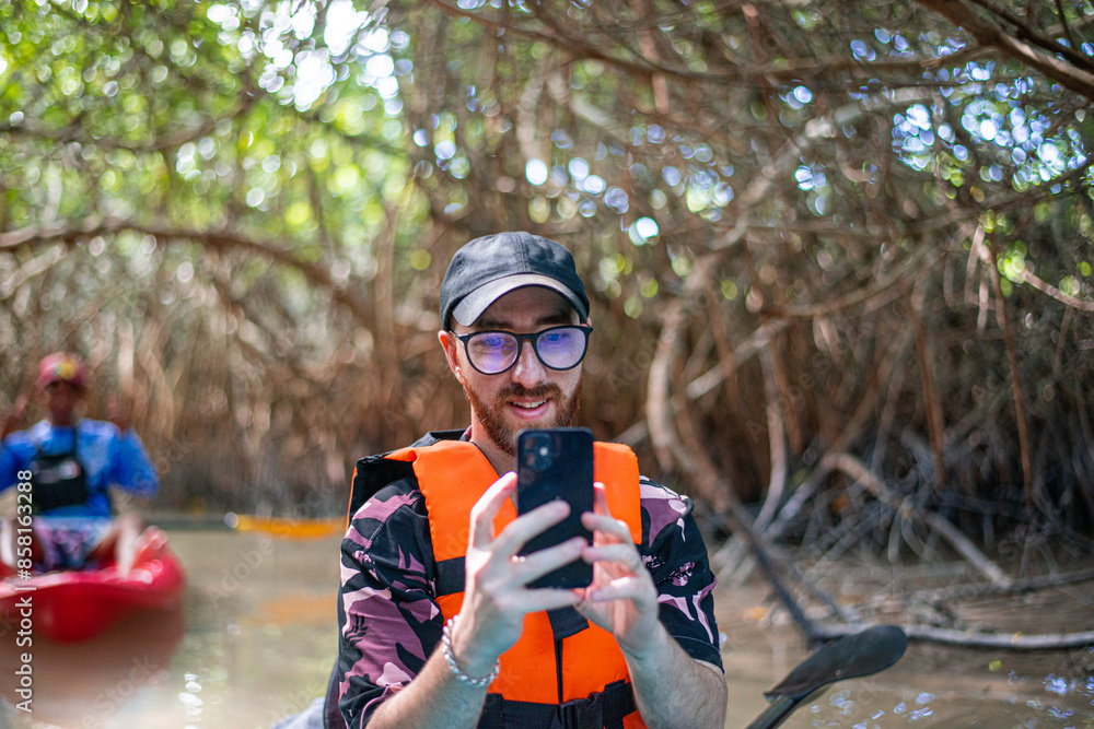 tourist with paddle in a blue kayak in a shallow sandy channel in dense ...