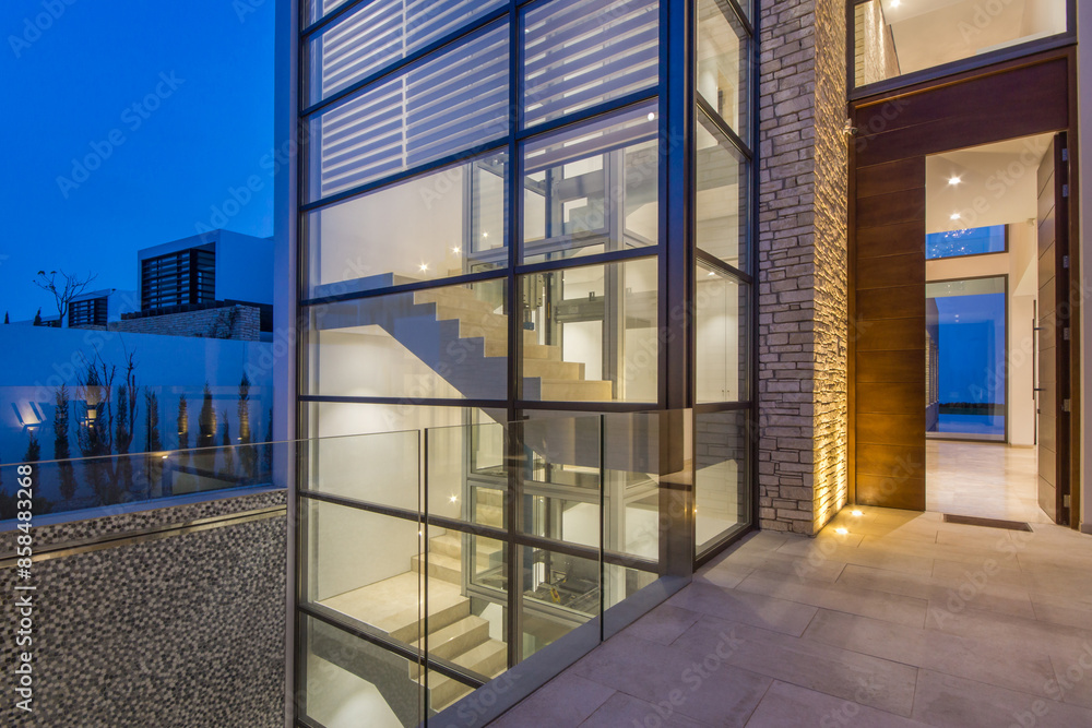 A modern home with a glass elevator and staircase is shown at night ...