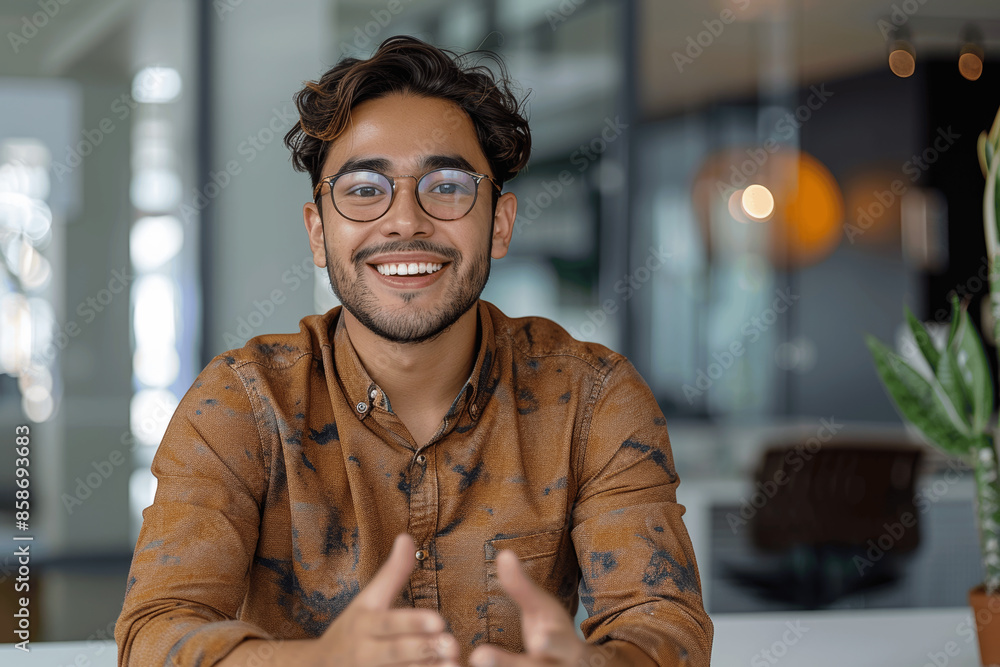 Happy young Latin man in glasses giving an interview in a modern office ...