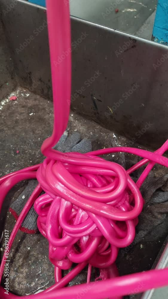 Pink rubber tubing melted being fed into a extrusion machine. The ...
