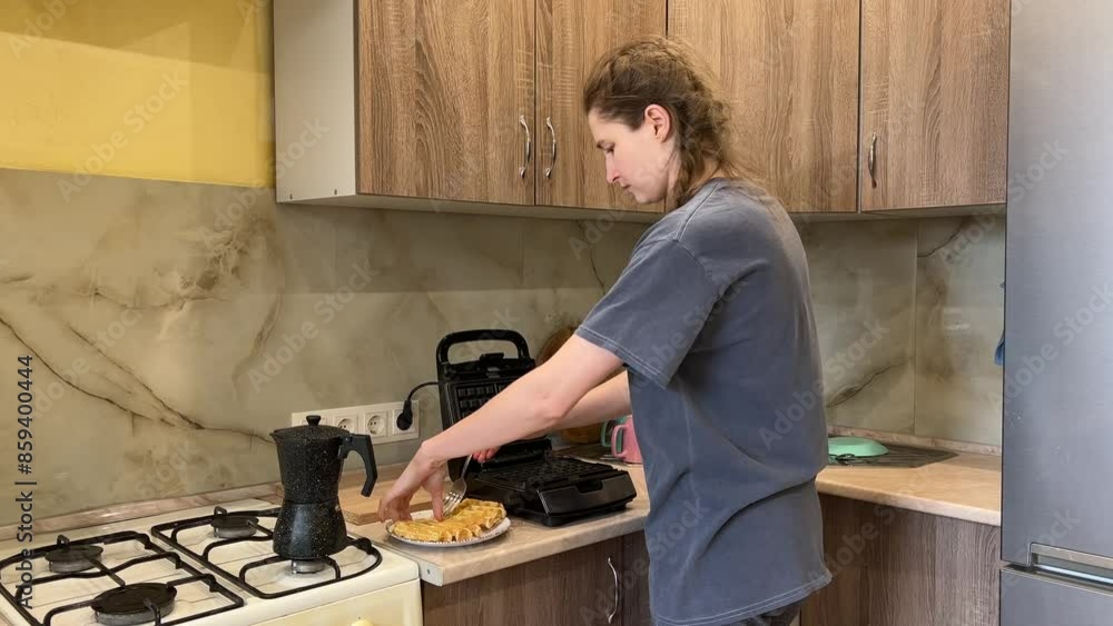Woman makes fresh waffles in a modern kitchen using a waffle maker. She ...
