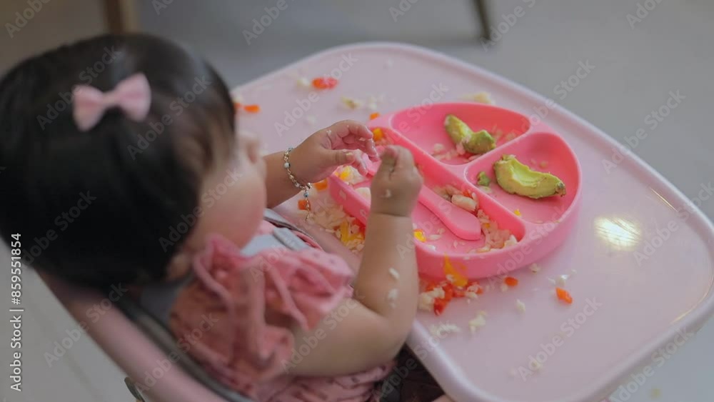 Little girl grabbing food from her plate with her hands while eating at ...