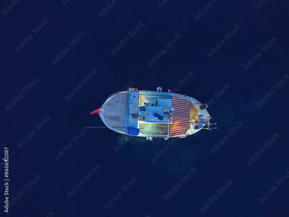 Aerial view of an illuminated fishing boat at night, floating on calm ...