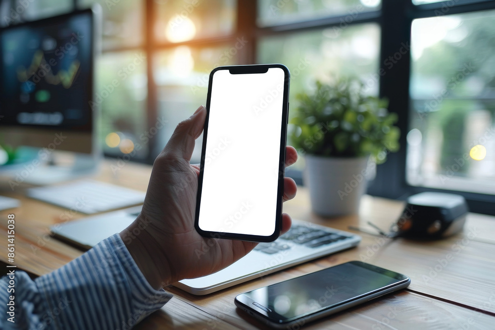 Hand holding a smartphone with a blank white screen in a modern office ...