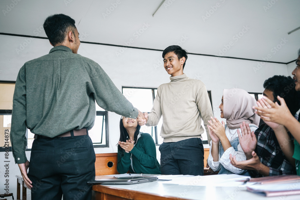 Asian male teacher shaking hands with high school student in classroom ...