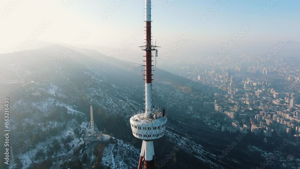 Tall TV tower placed on mountain with snow near modern urban district ...