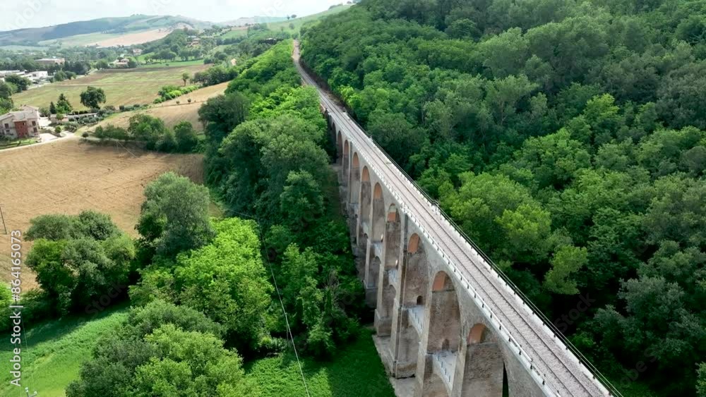 A drone flies over a long, stone railway viaduct in a rural area of ...