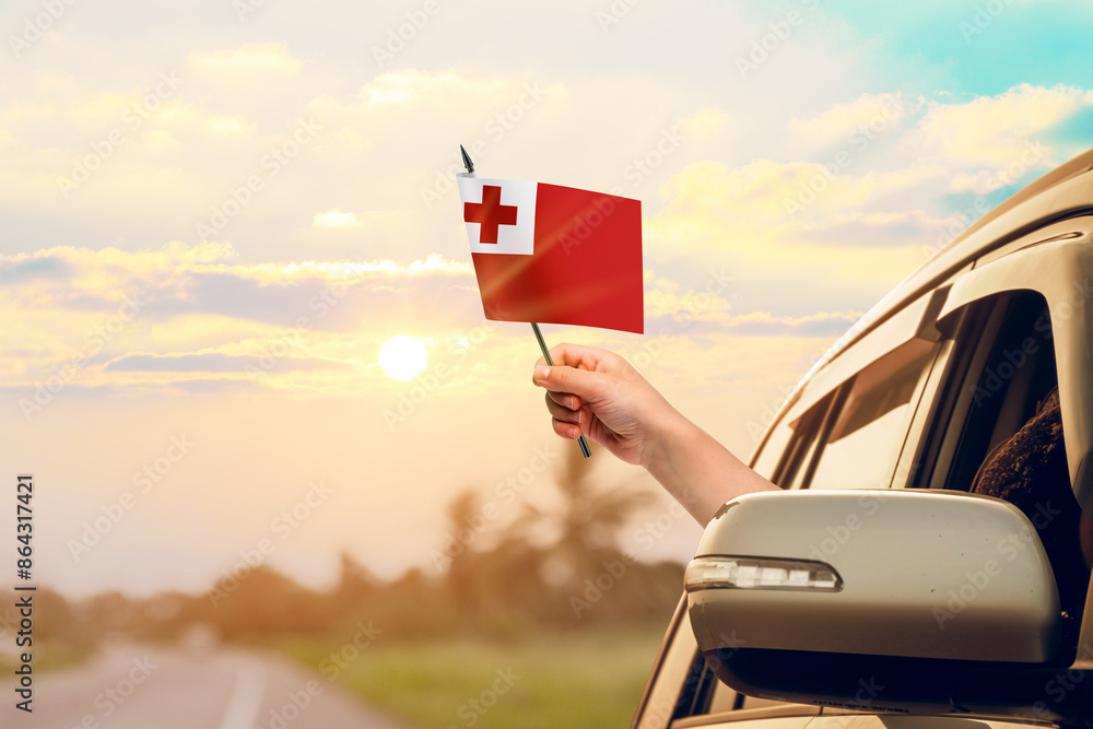 Waving the Tonga flag against the sunrise or sunset from a car driving ...