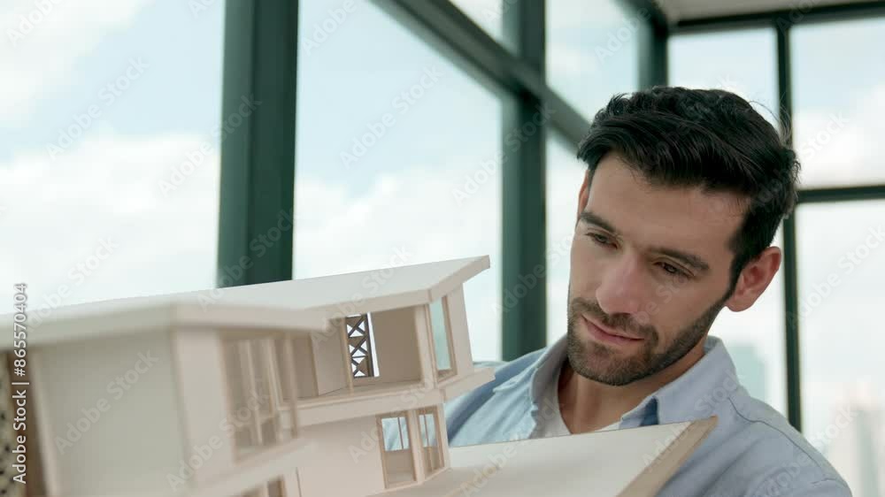 Skilled smiling caucasian engineer turns house model left and right to ...