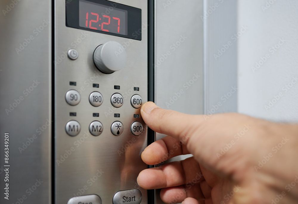Hand of an unrecognizable person operating the microwave, pressing the ...