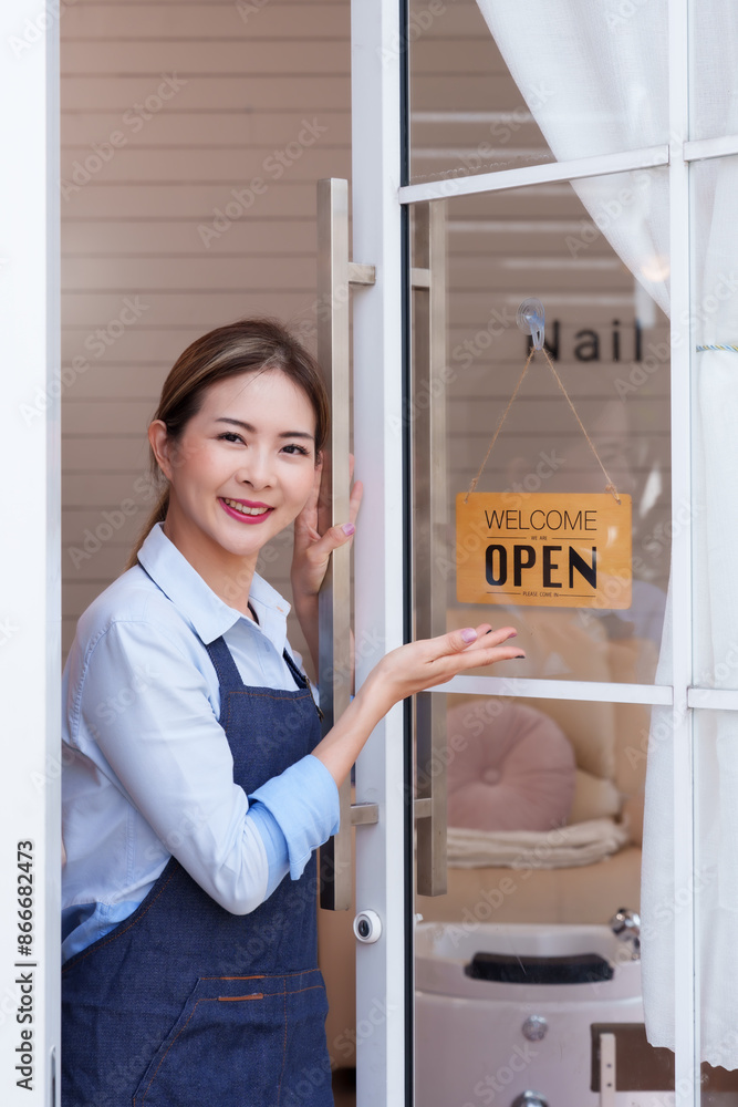 Asian female spa owner at spa entrance, smiling, wearing blue apron and ...
