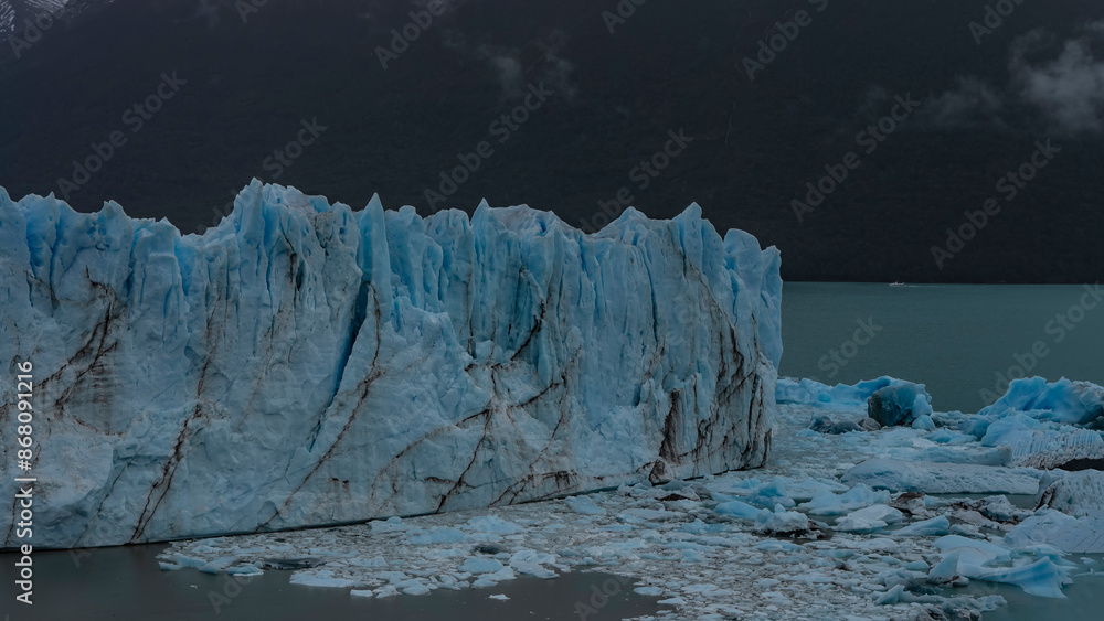 A wall of cracked blue ice with sharp peaks and crevices rises above ...