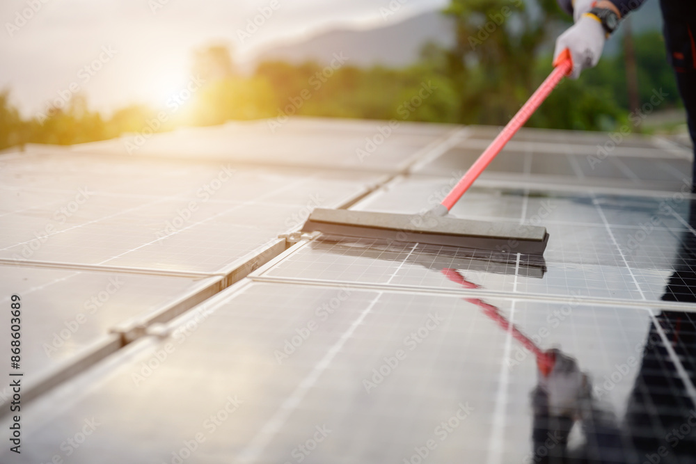 A worker maintaining solar energy systems cleans the solar panels on a ...