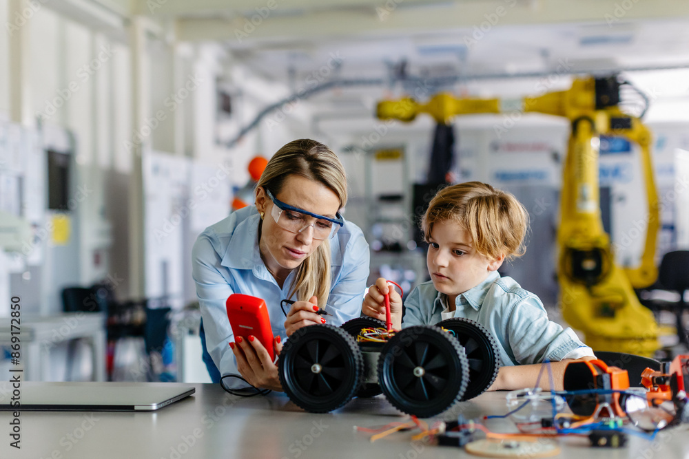 Female teacher helping young schoolboy to build robotic car in after ...