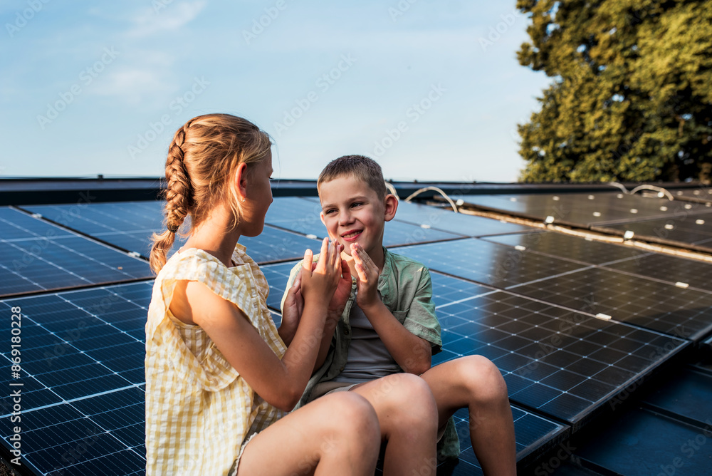 Two young siblings sitting on roof with solar panels, looking at each ...