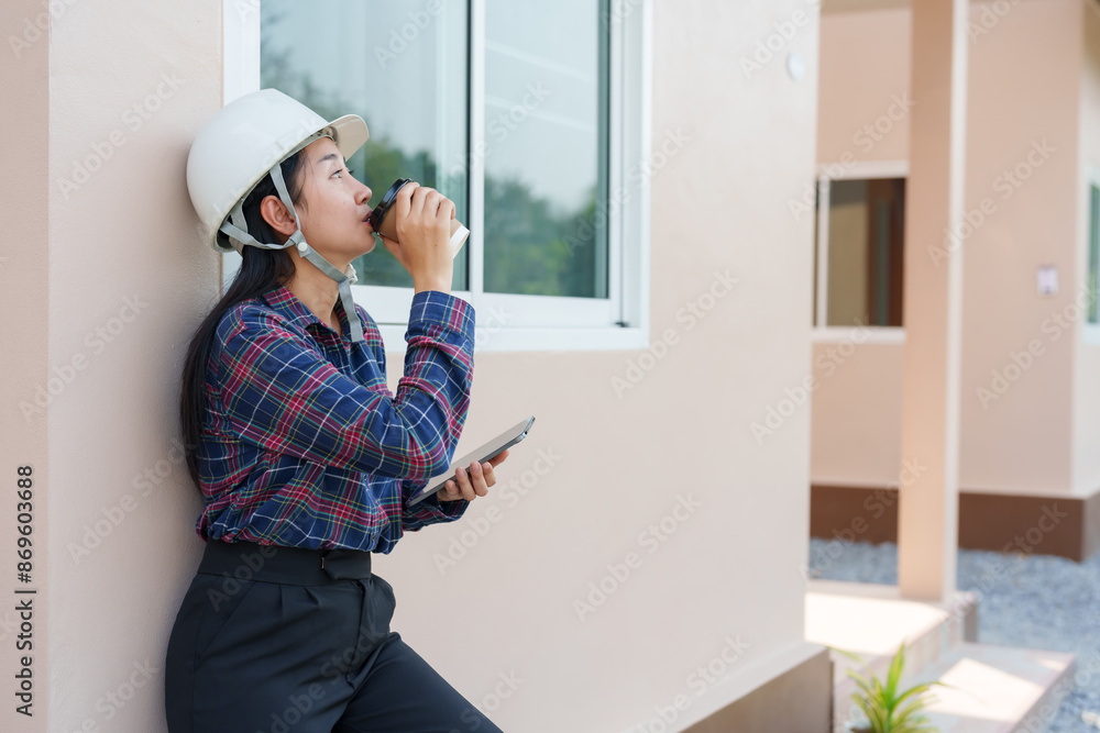 Asian female construction inspector drinking coffee while using tablet ...