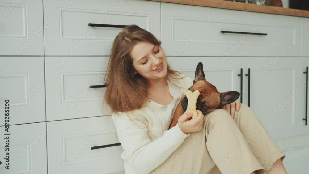 Woman sitting on kitchen floor with dog, offering treat while smiling ...