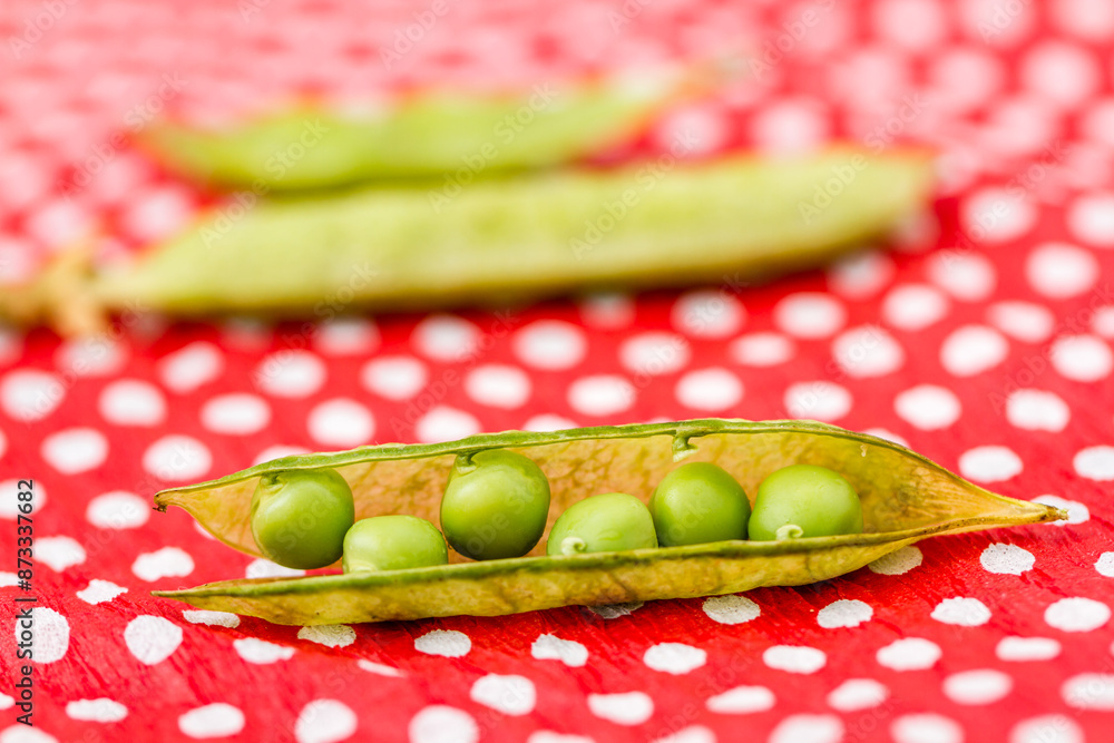 Open pea pod with green peas inside, placed on a red and white polka ...
