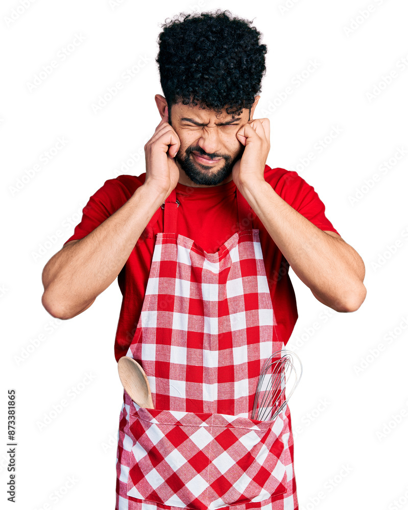 Young arab man with beard wearing cook apron covering ears with fingers ...