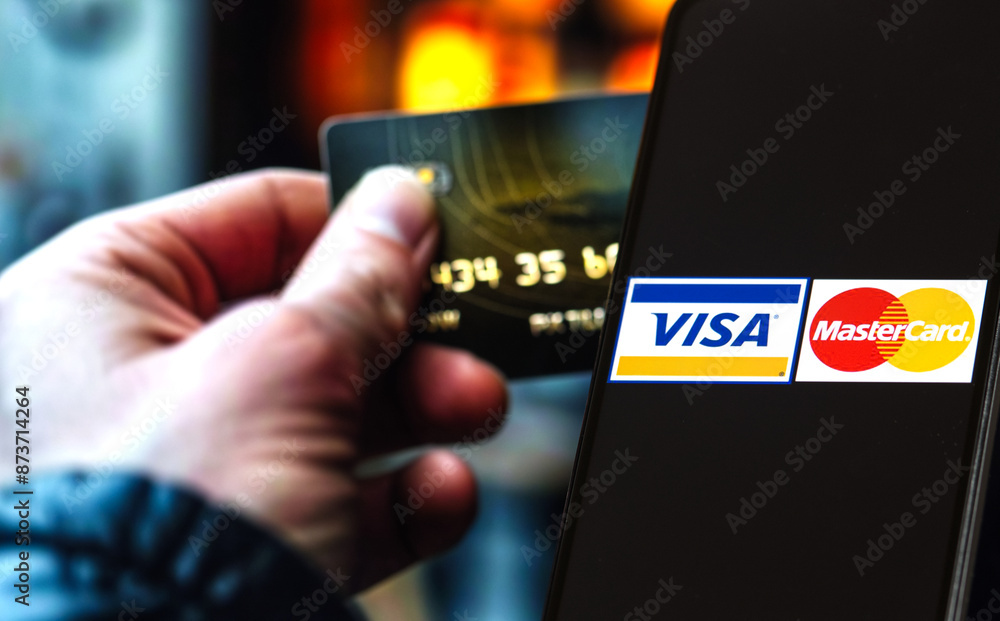 The logos of Mastercard and Visa are displayed on a smartphone, while a ...